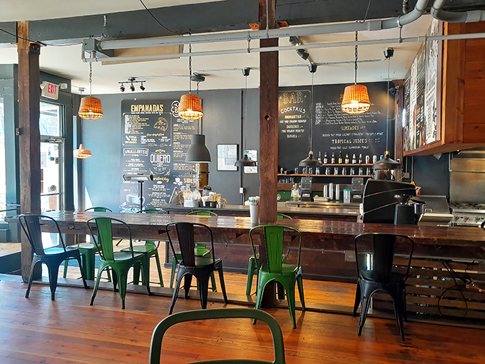 Interior: Warm wooden floors meet industrial chic at Quiero's counter, where colorful metal chairs add vibrant pops against sophisticated dark walls.