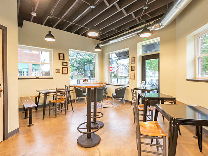 Sunlight streams through large windows, illuminating the minimalist interior where wooden tables and industrial touches create a space that invites lingering conversations.