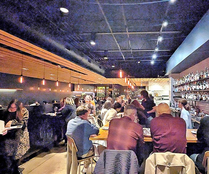 Interior: Warm wooden accents meet industrial chic in this buzzing dining room. Conversations flow as freely as the wine while diners lean into plates of deliciousness.