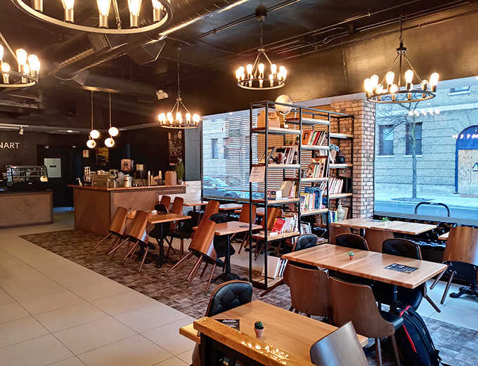Warm wooden tables, elegant chandeliers, and a bookshelf create the perfect atmosphere for lingering over coffee and pastries.