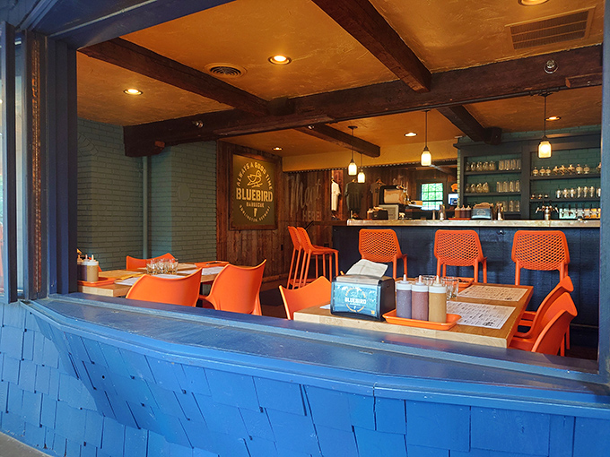 Rustic wooden beams meet modern orange seating in a space where comfort reigns supreme and barbecue aromas fill the air.