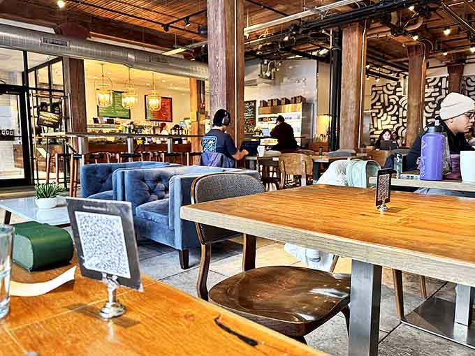 Exposed wooden beams meet plush blue seating in this industrial-chic interior where laptops and conversations find equal welcome.