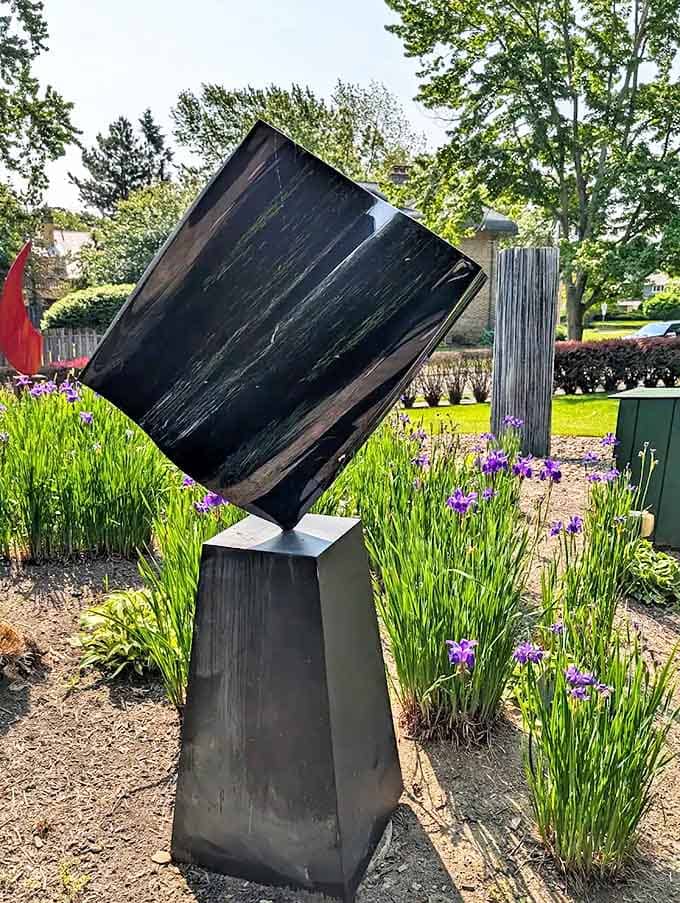 This enigmatic black monolith balances impossibly on its corner, surrounded by spring irises that soften its geometric precision.