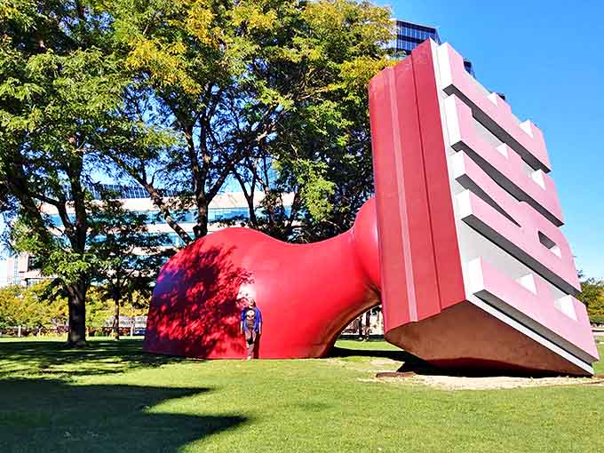 Nestled under the shade of trees, the Free Stamp's vibrant red base creates a striking contrast against the green canopy of Willard Park.