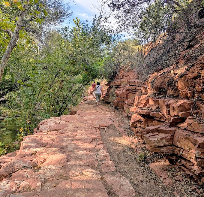 Hikers navigate the sun-dappled trail, where every step reveals new perspectives of Sedona's famous red sandstone landscape.