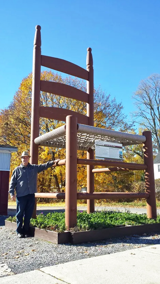 A visitor provides scale next to the mammoth chair, looking like he might be applying for a position as the giant's personal assistant or furniture dusting specialist.