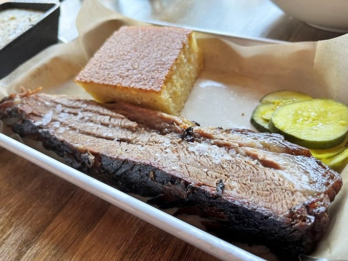 Brisket so tender it surrenders to your fork without a fight, accompanied by golden cornbread and house-made pickles &ndash; a plate that speaks the universal language of barbecue perfection.