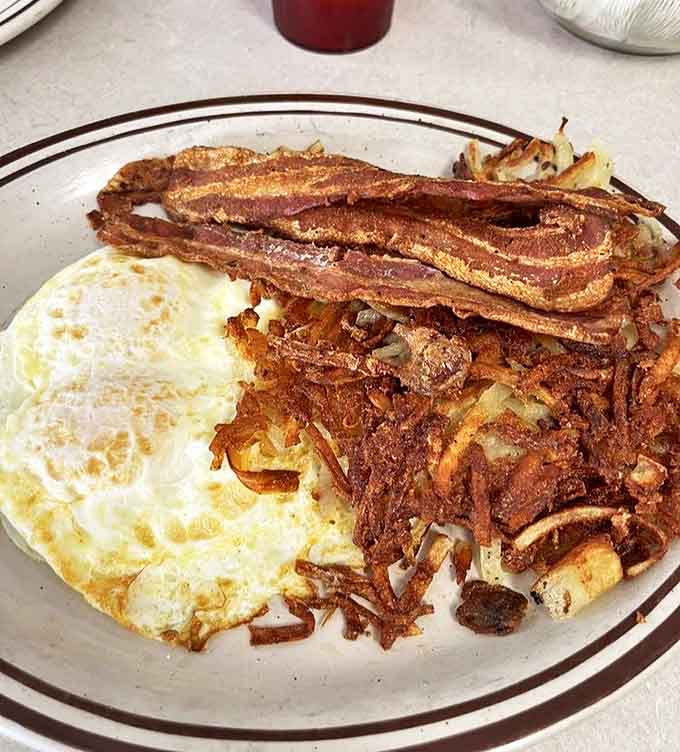 Breakfast perfection: crispy-edged hash browns supporting a sunny-side egg with bacon standing at attention like delicious sentinels.