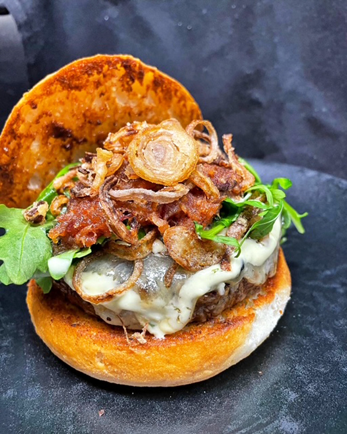 This isn't just a burger – it's a towering achievement of beef, cheese, greens and crispy onions that demands both hands and your full attention.