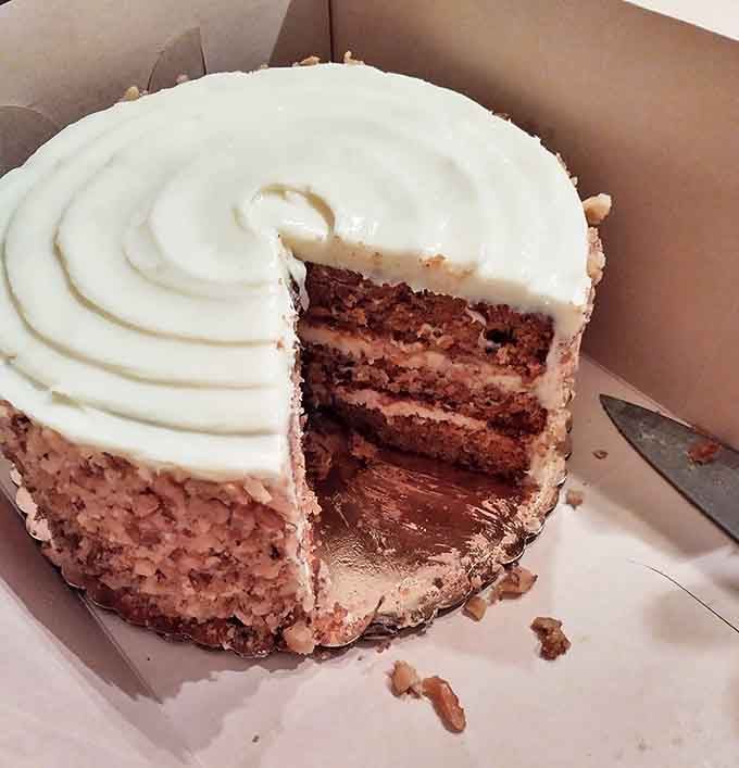 A slice of carrot cake perfection reveals its secrets: three moist layers, generous cream cheese frosting, and that telltale ring of chopped walnuts.