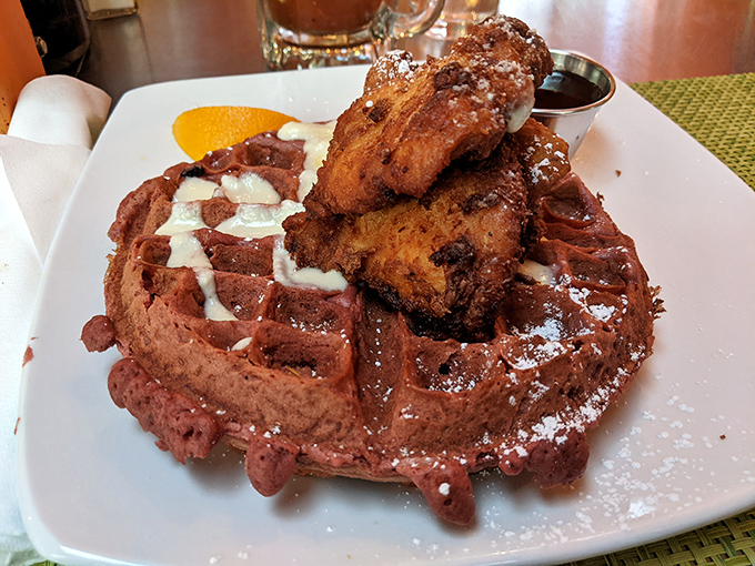 Behold the crown jewel: crispy beer-battered chicken perched atop a chocolate-red waffle, drizzled with maple syrup and dusted with powdered sugar.