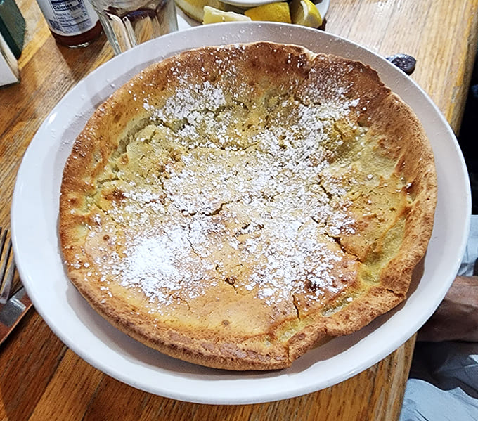The German Pancake arrives like edible sunshine, golden and puffy and dusted with enough powdered sugar to make your dentist nervous.