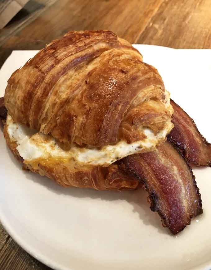 Behold the croissant sandwich in all its glory: flaky pastry, perfectly cooked egg, crispy bacon creating the breakfast trifecta that dreams are made of.