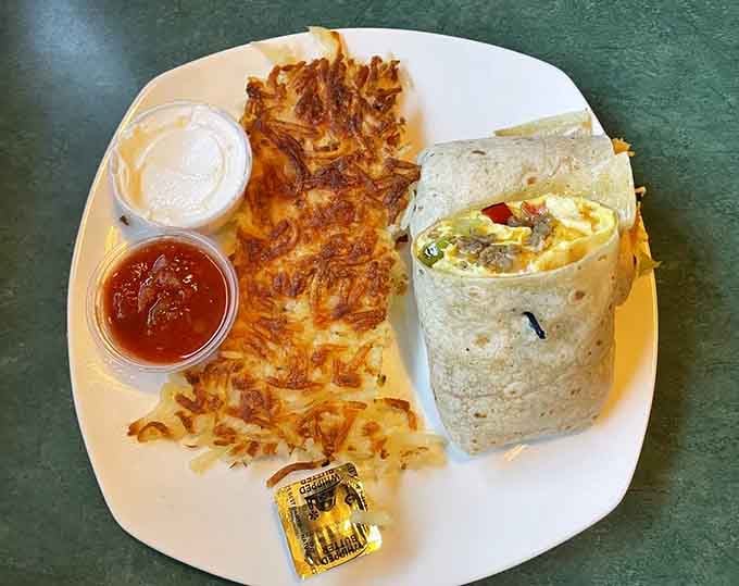 This breakfast burrito arrives wrapped and ready, stuffed with eggs, sausage, and cheese alongside perfectly crispy hash browns that crunch just right.