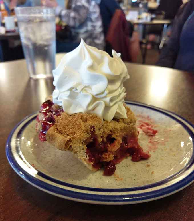 Raspberry rhubarb pie arrives looking almost too beautiful to eat, with that perfect balance of tart and sweet under a cloud of whipped cream.