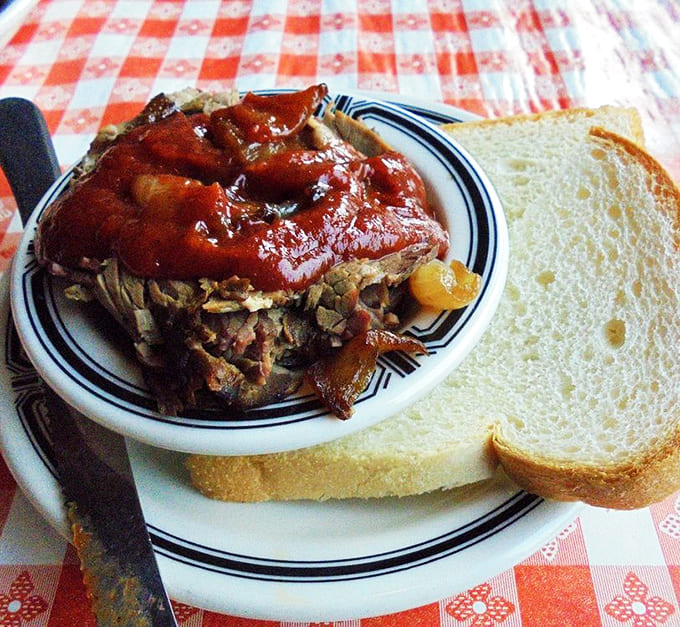 Behold the brisket in all its glory, tender meat glistening with sauce and served simply with white bread for soaking up every drop.