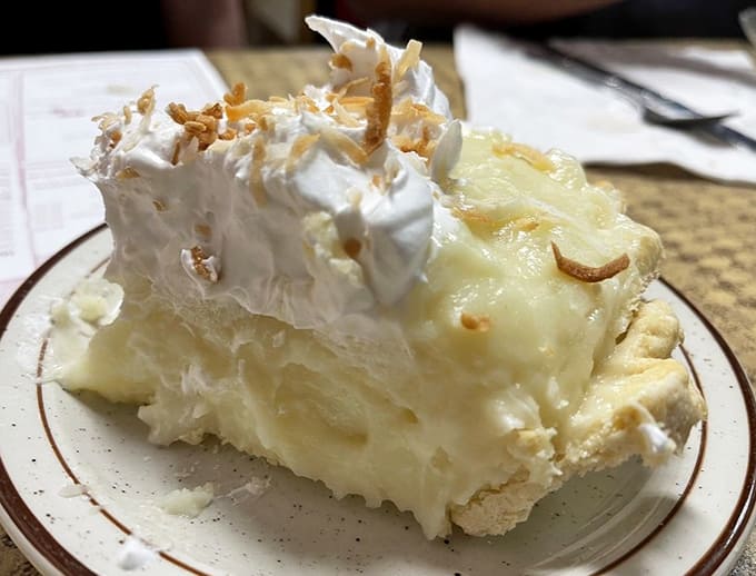 Coconut cream pie topped with toasted coconut and whipped cream, proof that heaven has a dessert menu and this is on it.