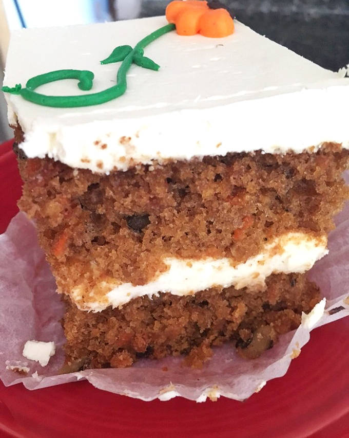 A perfect cross-section reveals the carrot cake's secrets: moist layers, generous frosting, and that signature decorative carrot on top.