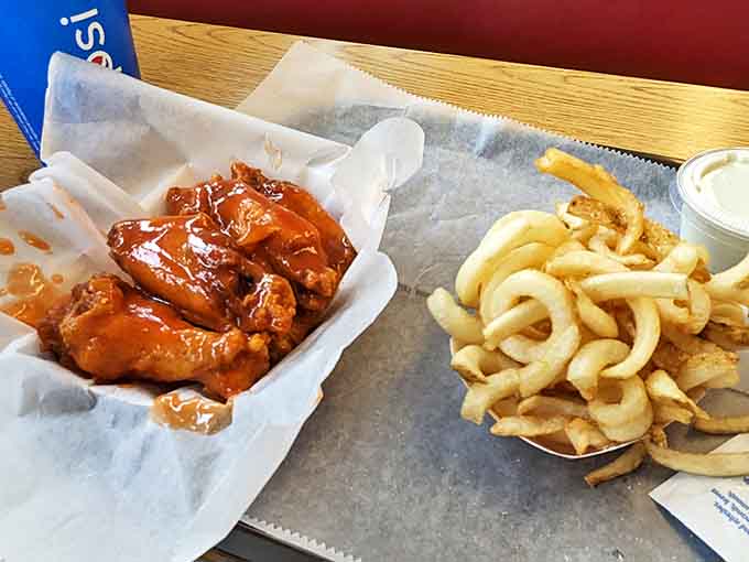The classic combo that launched a thousand napkins – gloriously sauced wings nestled beside golden curly fries. Perfection on paper.
