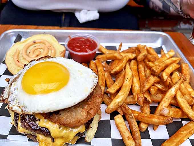 The Yo Mama Burger arrives crowned with a perfect sunny-side-up egg, its golden yolk ready to create the ultimate sauce for this towering masterpiece.