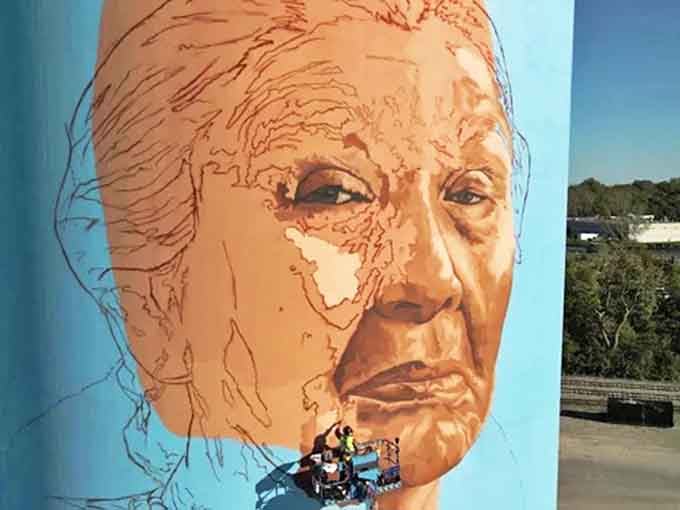 A weathered face tells stories of generations past, eyes gazing across the Maumee River with wisdom etched in every painted line.