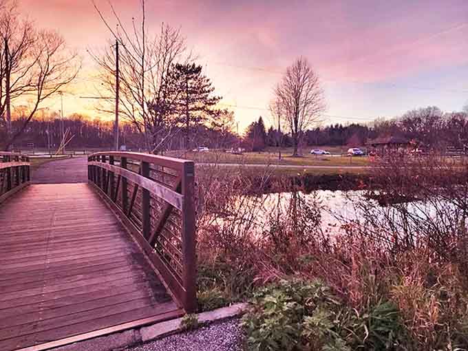 A rustic wooden bridge invites visitors to cross over calm waters while pink-streaked skies signal day's end.
