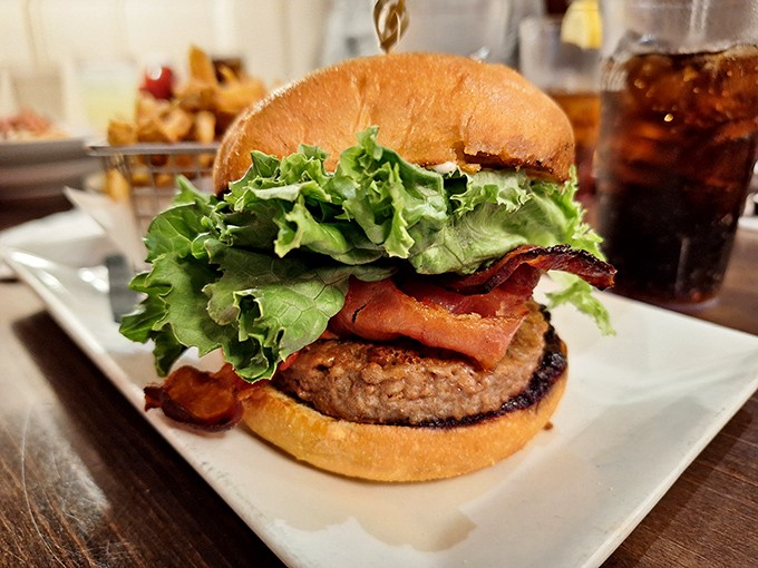 This isn't just any burger &ndash; it's a towering creation with crisp bacon, fresh lettuce, and a perfectly charred patty on a golden bun.
