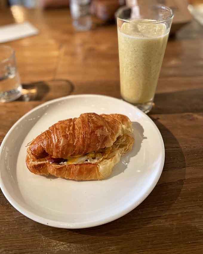 Two croissant sandwiches and colorful drinks prove that breakfast can be both indulgent and Instagram-worthy, though eating them is more important than photographing them.