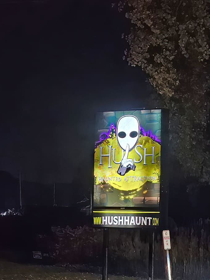 The Hush Haunted Attraction sign features their signature masked figure with a finger to its lips &ndash; a warning that some secrets are better left unspoken.