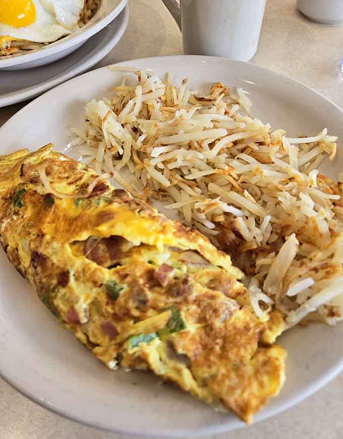 This omelet isn't messing around, arriving fluffy and loaded with fillings alongside those golden, crispy hash browns that dreams are made of.