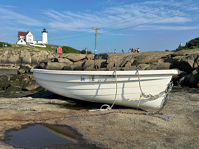 A weathered white boat rests on the rocks, perfectly positioned for countless visitor photos with the lighthouse backdrop.