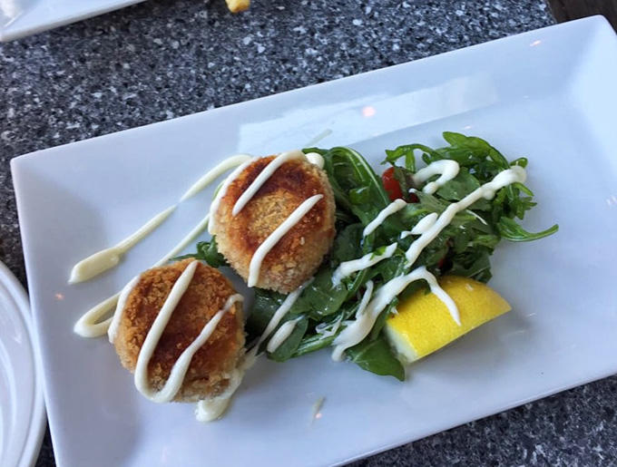 Golden-crusted lobster cakes arrive with a drizzle of sauce, proving that Maine knows how to treat its crustaceans right.