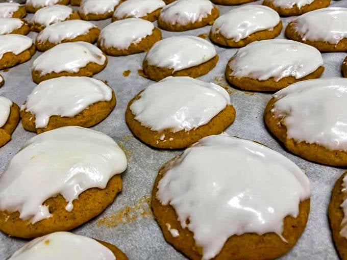 Fresh from the oven, these pumpkin cookies with their perfect white icing glisten like autumn sunshine, promising spiced comfort in every bite.