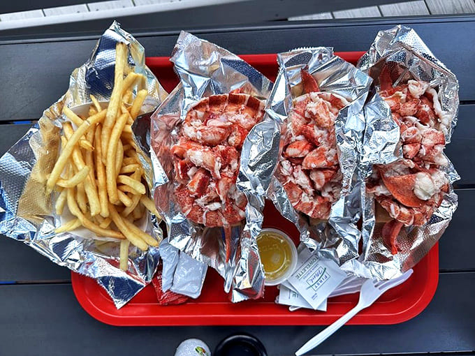 Three lobster rolls and fries spread across a tray like this is what happiness looks like when it's wrapped in foil.