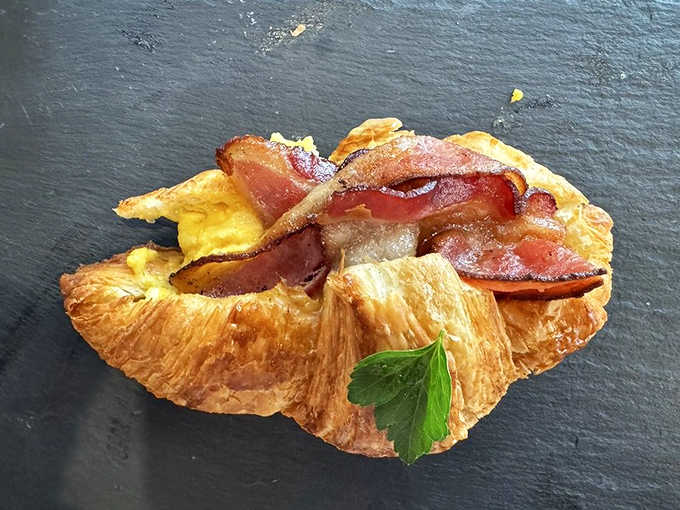 Morning indulgence: Crispy bacon, fluffy eggs, and fresh vegetables nestled in a buttery croissant that shatters with each heavenly bite.
