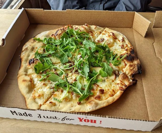 Fresh arugula piled high on a white pizza proves that sometimes simple ingredients and a wood-fired oven are all you need for perfection.