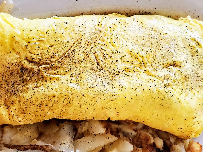 A perfectly executed omelet reveals its golden exterior while hiding a treasure of fillings within &ndash; breakfast architecture at its finest.
