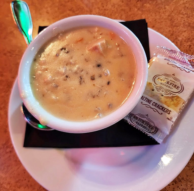 A humble cup of wild rice soup arrives with saltine crackers, proving that sometimes the simplest combinations deliver the most profound comfort.