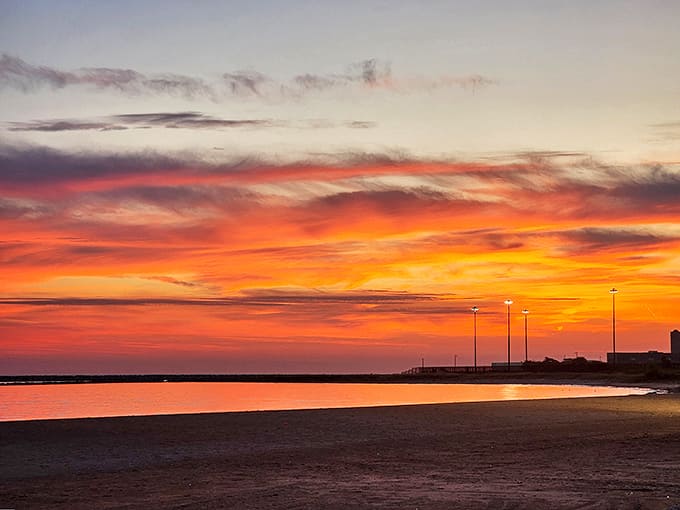 The sky performs its nightly masterpiece as sunset paints Rainbow Beach in dramatic oranges and pinks, reflecting off the calm lake surface.