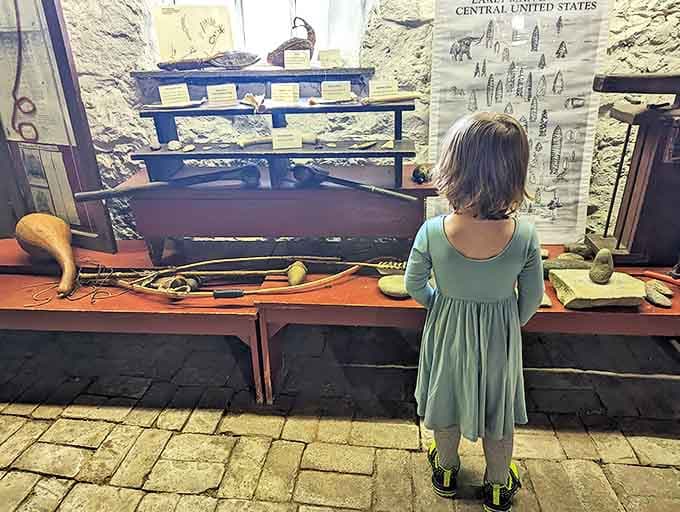 A young visitor contemplates Native American artifacts, bridging centuries as she connects with tools once held by the region's first inhabitants.