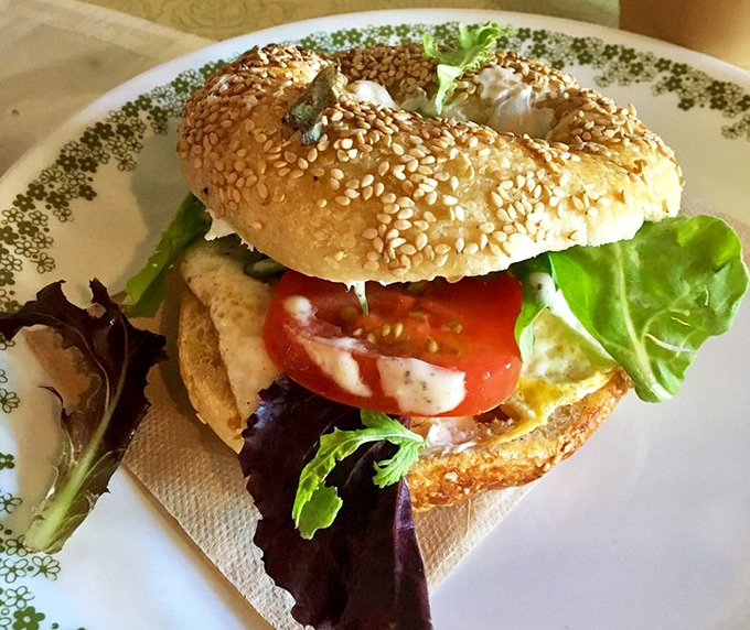 A masterpiece of balance &ndash; creamy avocado, vibrant tomato, and fresh greens nestled between perfectly toasted bagel halves.
