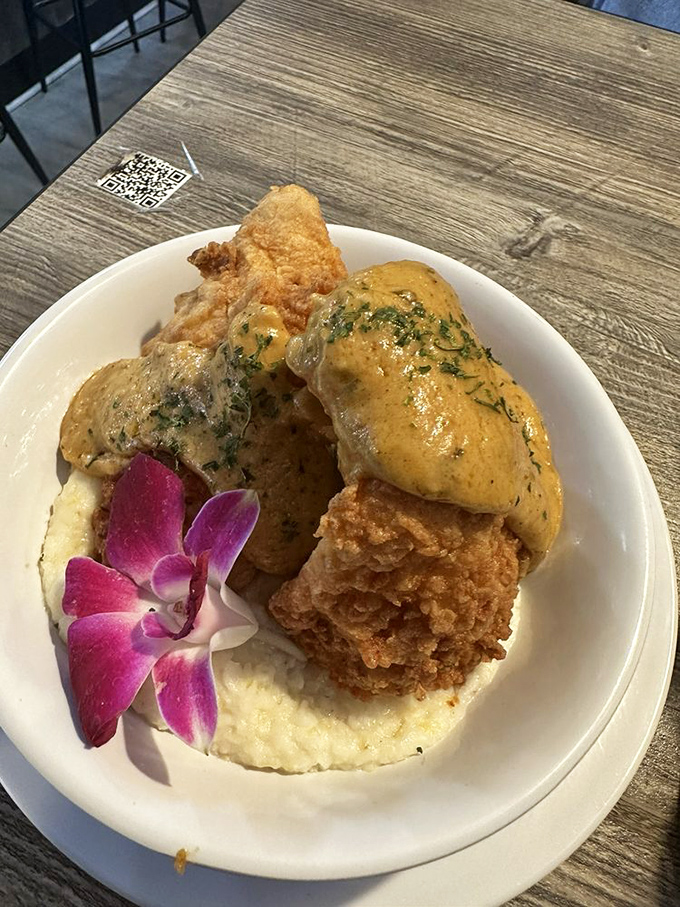 Southern fried catfish over creamy grits topped with Cajun sauce &ndash; a textural masterpiece where crispy meets creamy in perfect harmony.
