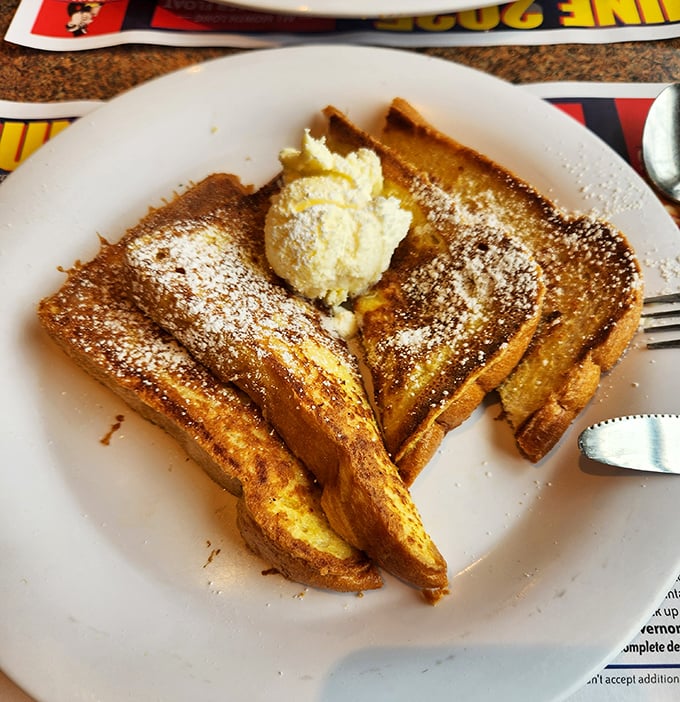 French toast that's achieved golden perfection, dusted with powdered sugar and waiting for its maple syrup waterfall moment.