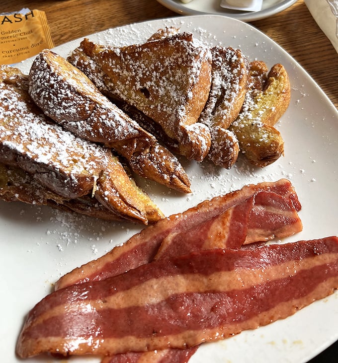 Golden challah French toast dusted with powdered sugar alongside perfectly crisp bacon &ndash; breakfast doesn't get better than this!