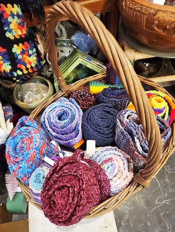 Hand-knitted scarves nestled in a basket showcase craftsmanship that defies our disposable culture – each colorful coil representing hours of patient creation.