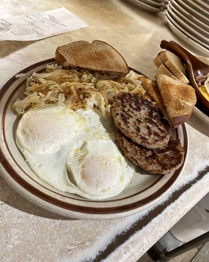 The classic breakfast plate delivers everything you need: eggs cooked just right, savory sausage, crispy hash browns, and perfectly buttered toast.
