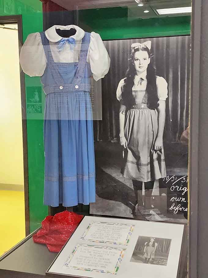 The blue gingham dress hangs beside a photograph of young Judy, connecting costume to the girl who made it iconic.