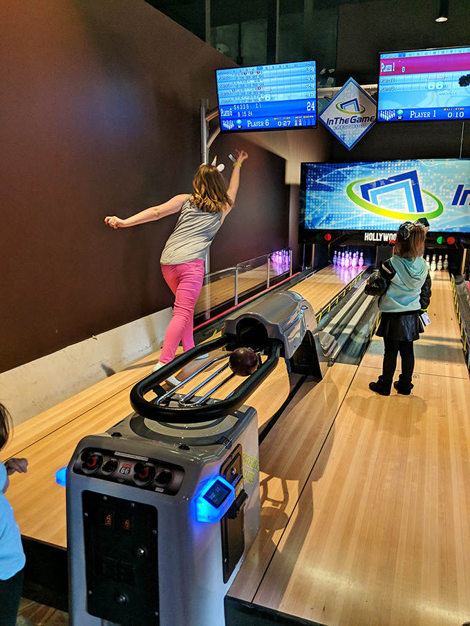 A young bowler celebrates her throw with unbridled joy, the modern bowling setup perfectly sized for smaller competitors.
