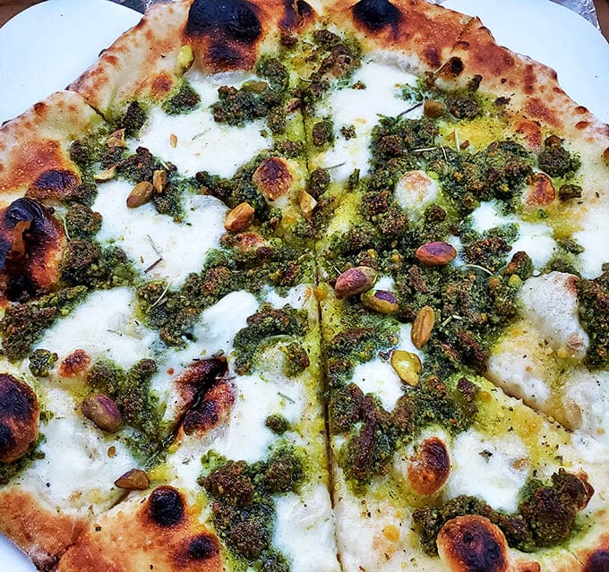 A verdant landscape of basil pesto dotted with pine nuts creates a pizza experience that's both familiar and excitingly new.