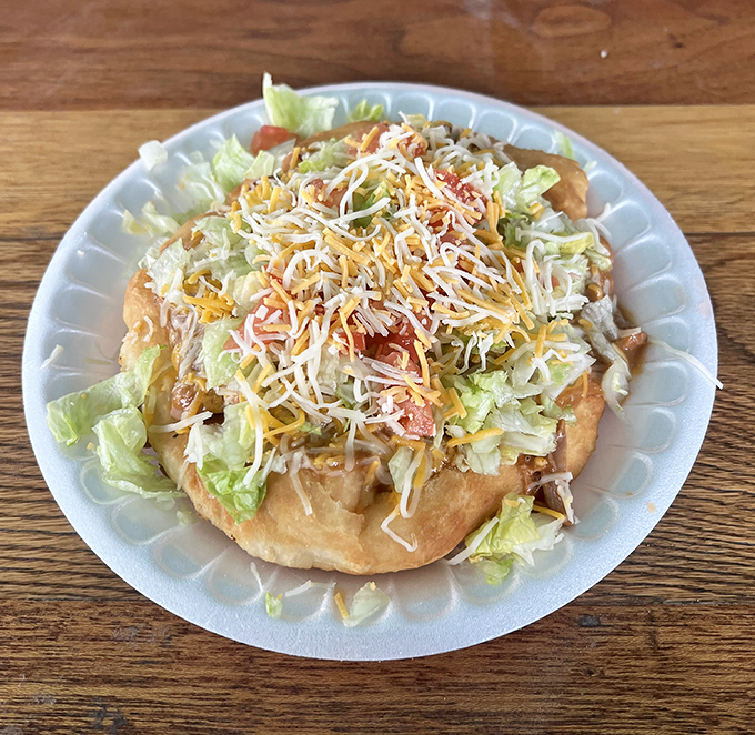 A mountain of red chili and beans cascades over perfectly fried dough, creating a knife-and-fork affair that rewards every single bite.